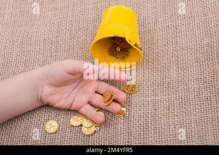 Bucket and fake gold coins in hand on canvas background Stock Photo - Alamy