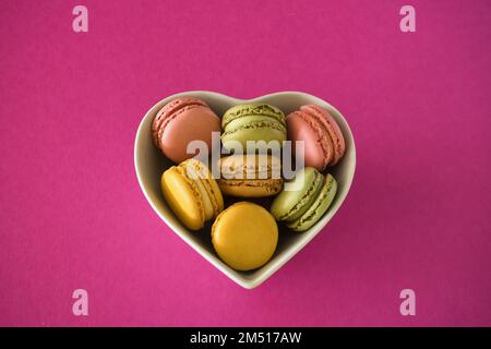 A gift with colorful macaroons inside a heart-shaped box on a hot pink ...