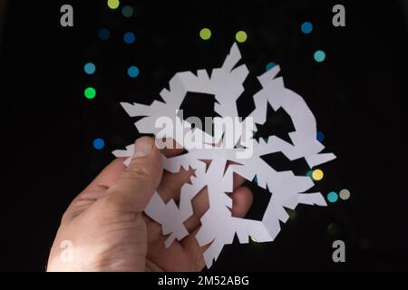 Snowflake shaped paper in hand on bokeh light background Stock Photo ...