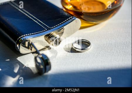 Black and silver whiskey flask next to a glass of amber colored liquid ...