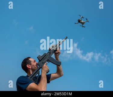 A man aims to shoot a rifle at a flying drone against a blue sky Stock ...