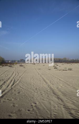 Sandy rivershore dotted by bushes with a bridge over the river on the ...