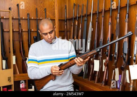 Interested man choosing hunting rifle in gun shop Stock Photo - Alamy