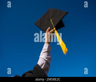 Close-up of a woman's hand with a graduation cap against the blue sky ...