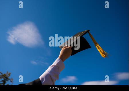 Close-up of a woman's hand with a graduation cap against the blue sky ...