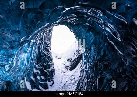 Ice cave open to the top with snow-covered ice combs, black and white ...