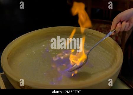 Flambe of Italian brandy lit on fire in pecorino wheel to soften the ...