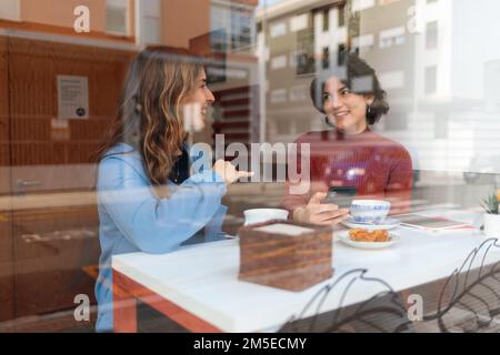 The two women visible through window glass sitting in the cafe ...