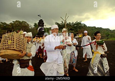 A Balinese clan is walking on sandy beach to conduct a ritual to honor ...