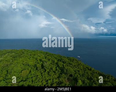 A bright rainbow appears behind a remote tropical island in the Solomon ...