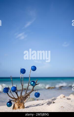 Dead corals decorated with blue Christmas balls standing on the sand ...