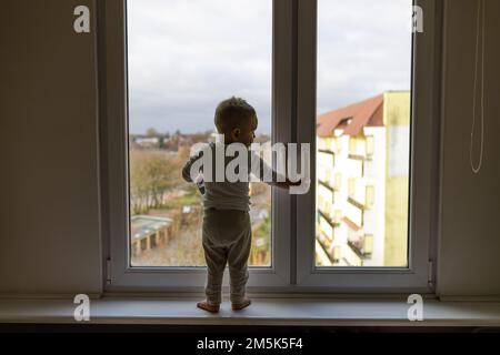 Lonely child standing on the windowsill. Dangerous situation, risk of ...