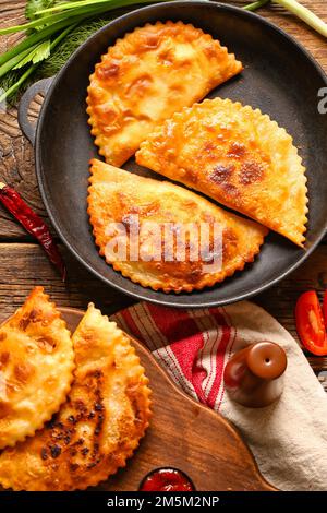 Frying pan with tasty chebureks on wooden background Stock Photo - Alamy