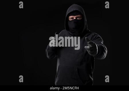 Masked robber with gun aiming into the camera against a black ...