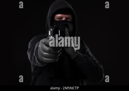Masked robber with gun aiming into the camera against a black ...