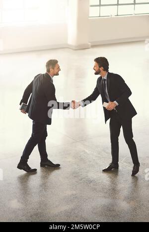 Making deals. two businesspeople shaking hands in an office while a ...