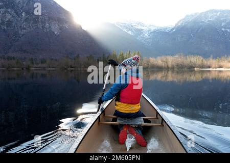 Boy paddling in a canoe in winter time on lake Bohinj in Triglav ...