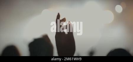 A silhouette of the raised hands at a big event with a blurred ...