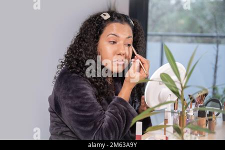 Concentrated Hispanic female with curly dark hair applying brown ...