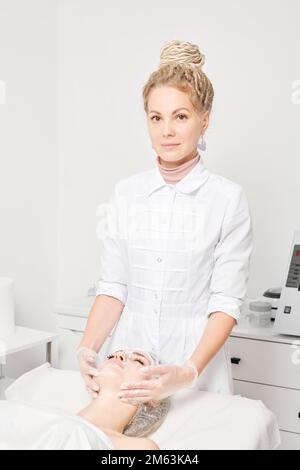 Cosmetologist massages cream mask into woman face skin for rejuvenation ...