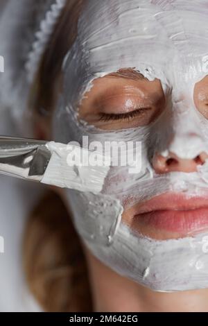 Cosmetologist applying clay mask on man's face in spa salon. Side view ...