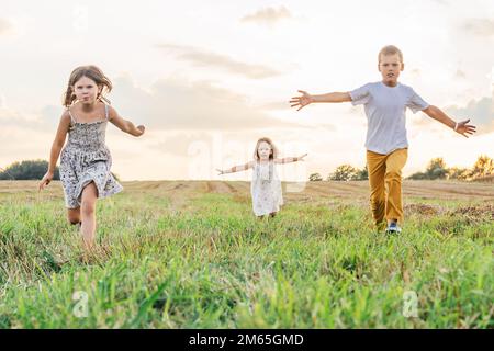 Happy little children joyfully run forward across field waving arms ...