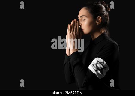 Young woman with armband praying on black background. International ...