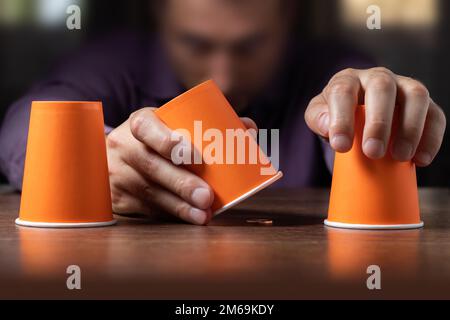 Man shows shell game of thimbles with coin, dark background. Concept ...