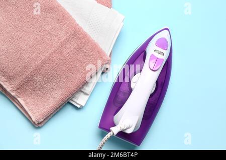 Stack of towels and electric iron on light blue background Stock Photo ...