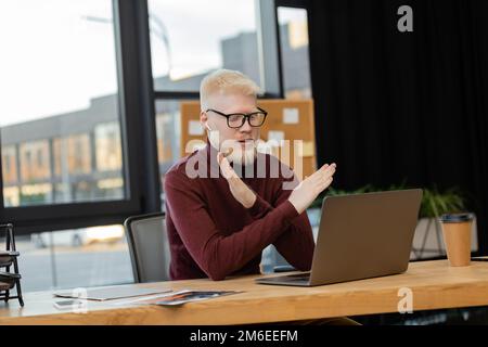 bearded albino businessman in earphones looking at laptop while working ...