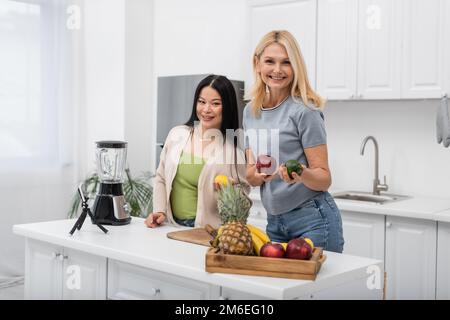 Cheerful multiethnic bloggers looking at cellphone in ring lamp near ...