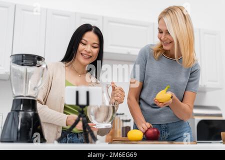 Multiethnic bloggers holding organic fruits near smartphone and ring ...