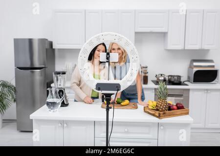 Interracial bloggers cutting fresh fruits near blender and smartphone ...