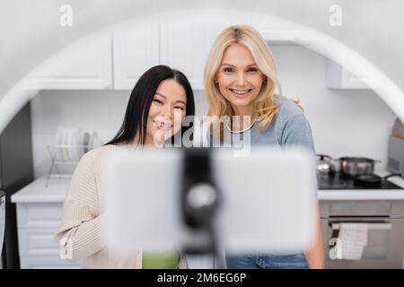 Cheerful multiethnic bloggers looking at cellphone in ring lamp near ...