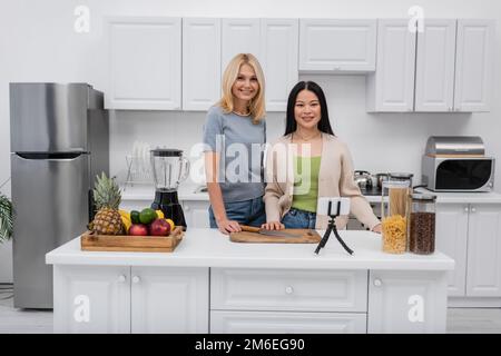 Positive interracial bloggers looking at smartphone in ring lamp near ...
