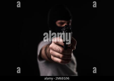 Masked robber with gun aiming into the camera against a black ...