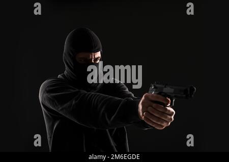 The robber in a mask with a gun pointed to the side on a black ...