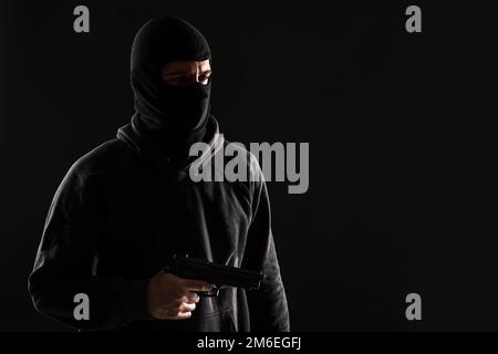 The robber in a mask with a gun pointed to the side on a black ...