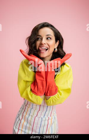 coquettish housewife in red rubber gloves and apron smiling and holding ...