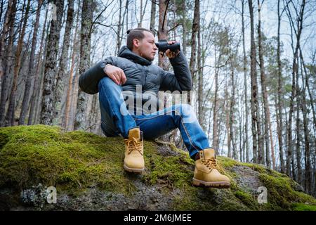 Traveler with monocle sitting on big stone in deep forest and looks ...