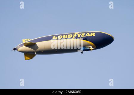 A Goodyear Blimp flies overhead. Spectators and floats line the streets ...