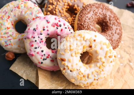 Sheet of baking paper with tasty donuts and nuts on dark background ...