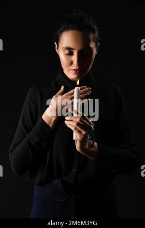 Young woman with candle and military tag praying on black background ...