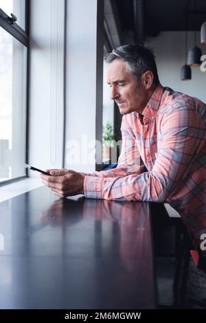 Mature businessman text messaging through mobile phone sitting in cafe ...