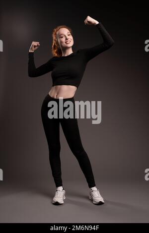 Content young sportswoman standing in studio with open belly show arms ...