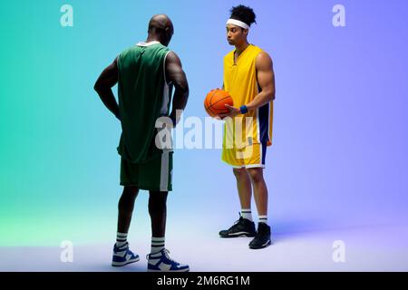 Image of two diverse basketball players with basketball on purple to ...