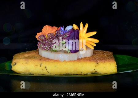 Fried polenta slice with a slice of lotus root and meadow flowers as ...