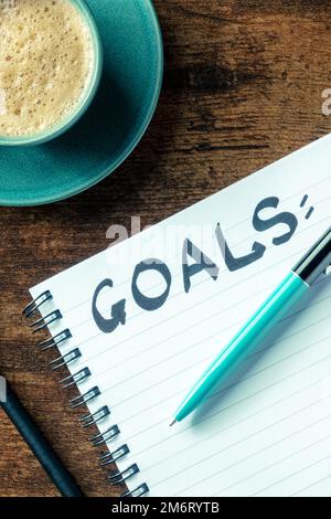 Goals, handwritten word in a notepad with a ballpoint pen and a cup of ...