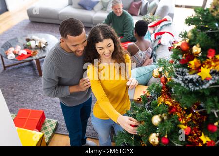 Happy diverse female friends decorating christmas tree at christmas ...