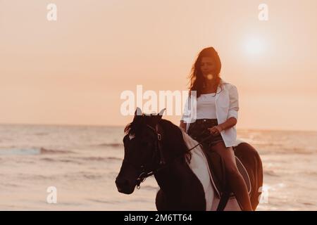 Woman in summer clothes enjoys riding a horse on a beautiful sandy ...
